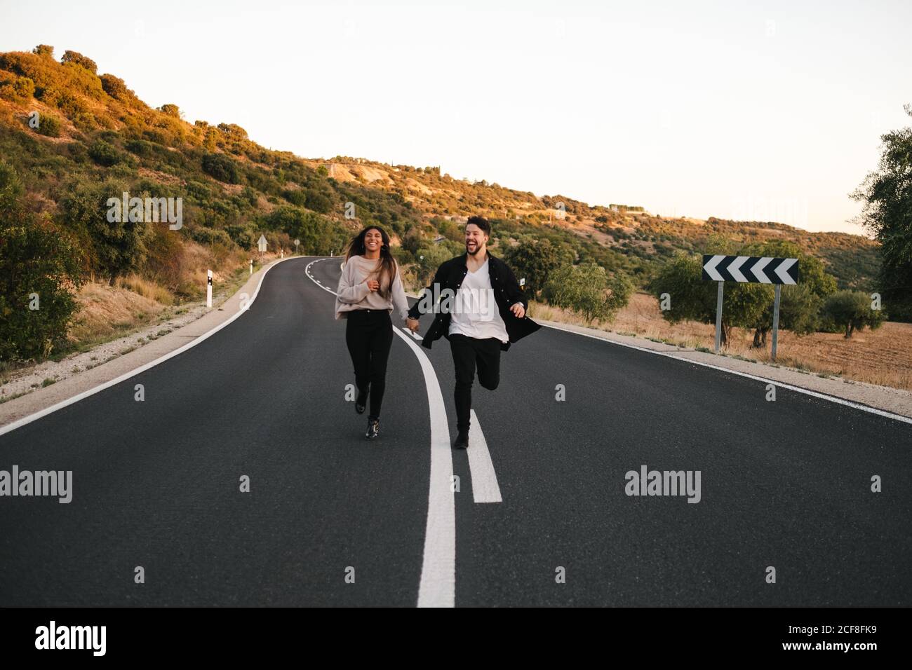 Stylish boyfriend and girlfriend running along empty roadway in ...