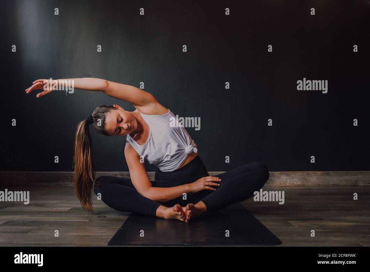 Young relaxed female with eyes closed and arm raised sitting in baddha ...