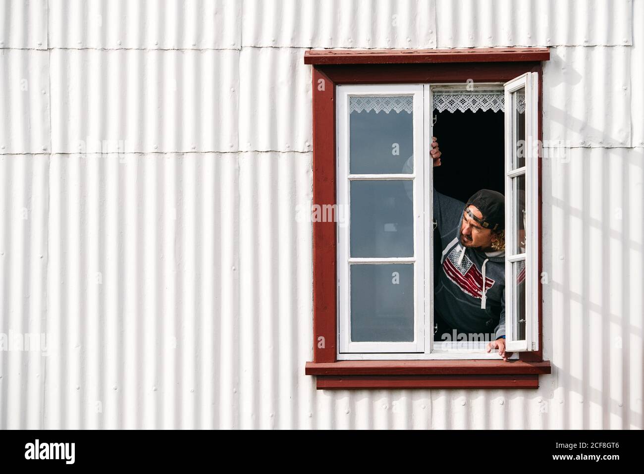 Male leaning on windowsill and looking out of window of residential ...