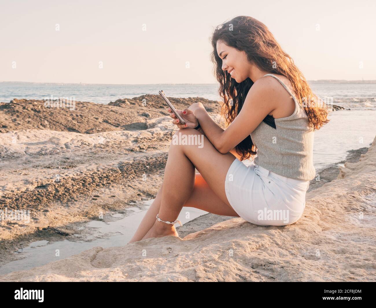 Dreamy trendy young ethnic Woman texting on beach Stock Photo - Alamy