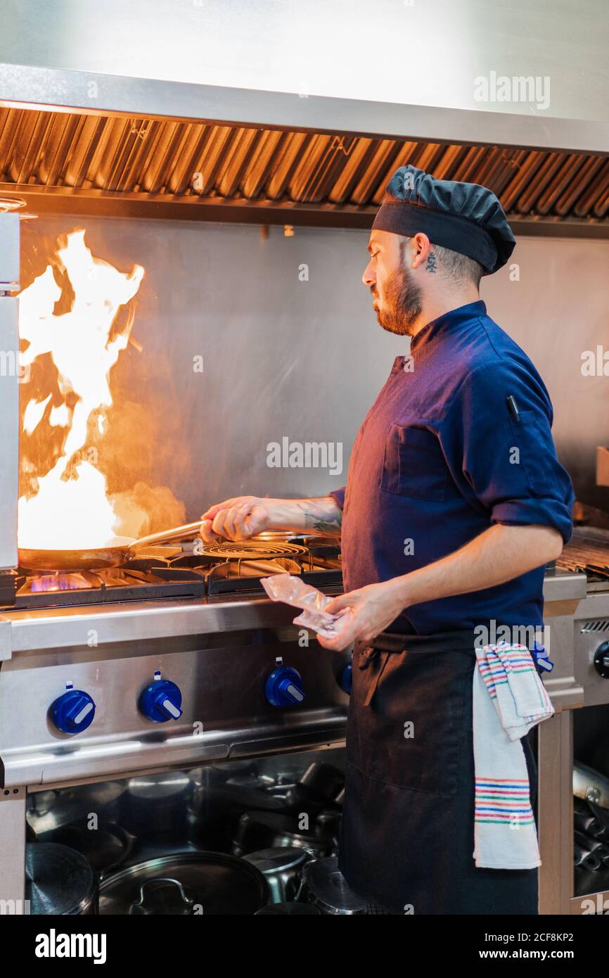 Side view of male cook doing flambe on food while standing at gas stove ...
