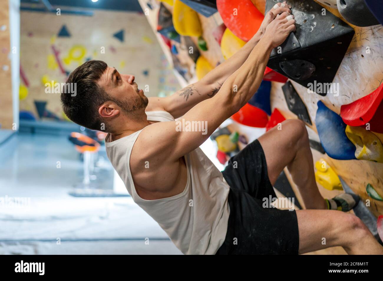 Side view of strong male athlete in sportswear climbing on colorful ...