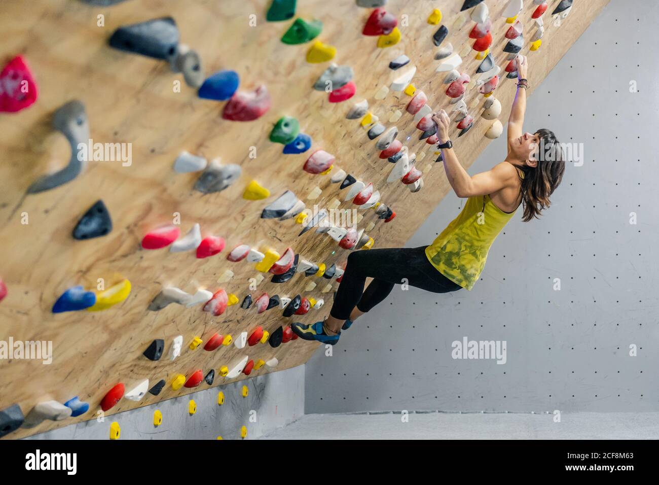 Side view from below of focused Woman in sportswear hanging on steep ...