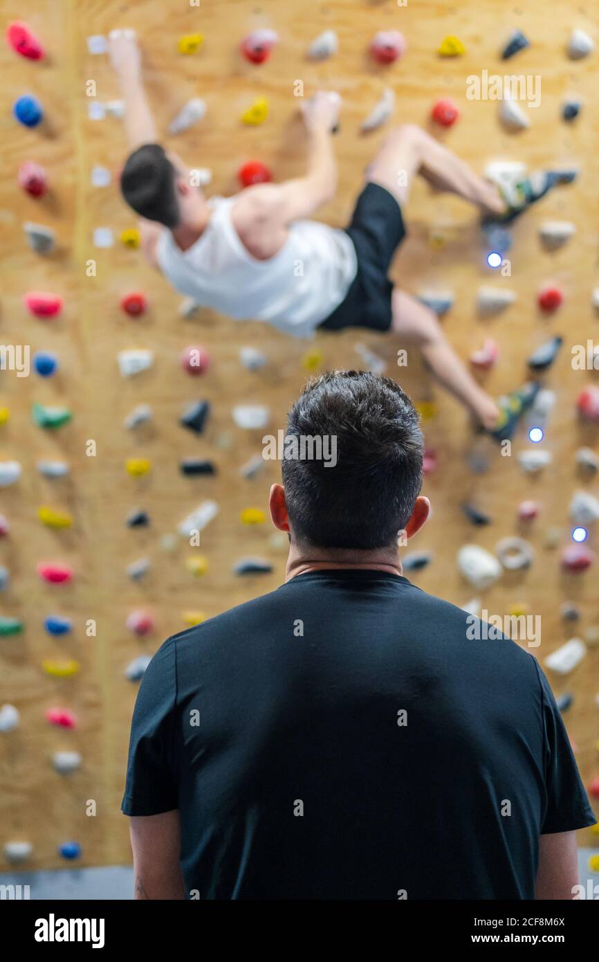 Back view of anonymous male athlete in sportswear watching for climber ...