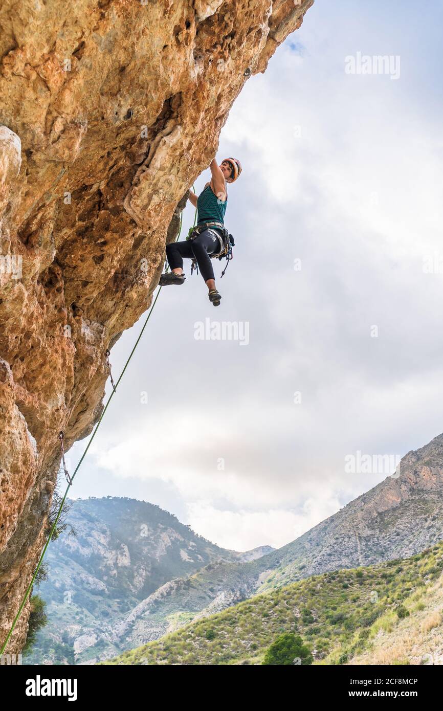 From below faceless sportive female alpinist climbing on sheer cliff in ...