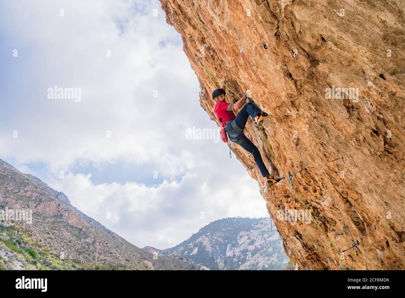 From below faceless sportive male alpinist climbing on sheer cliff in ...