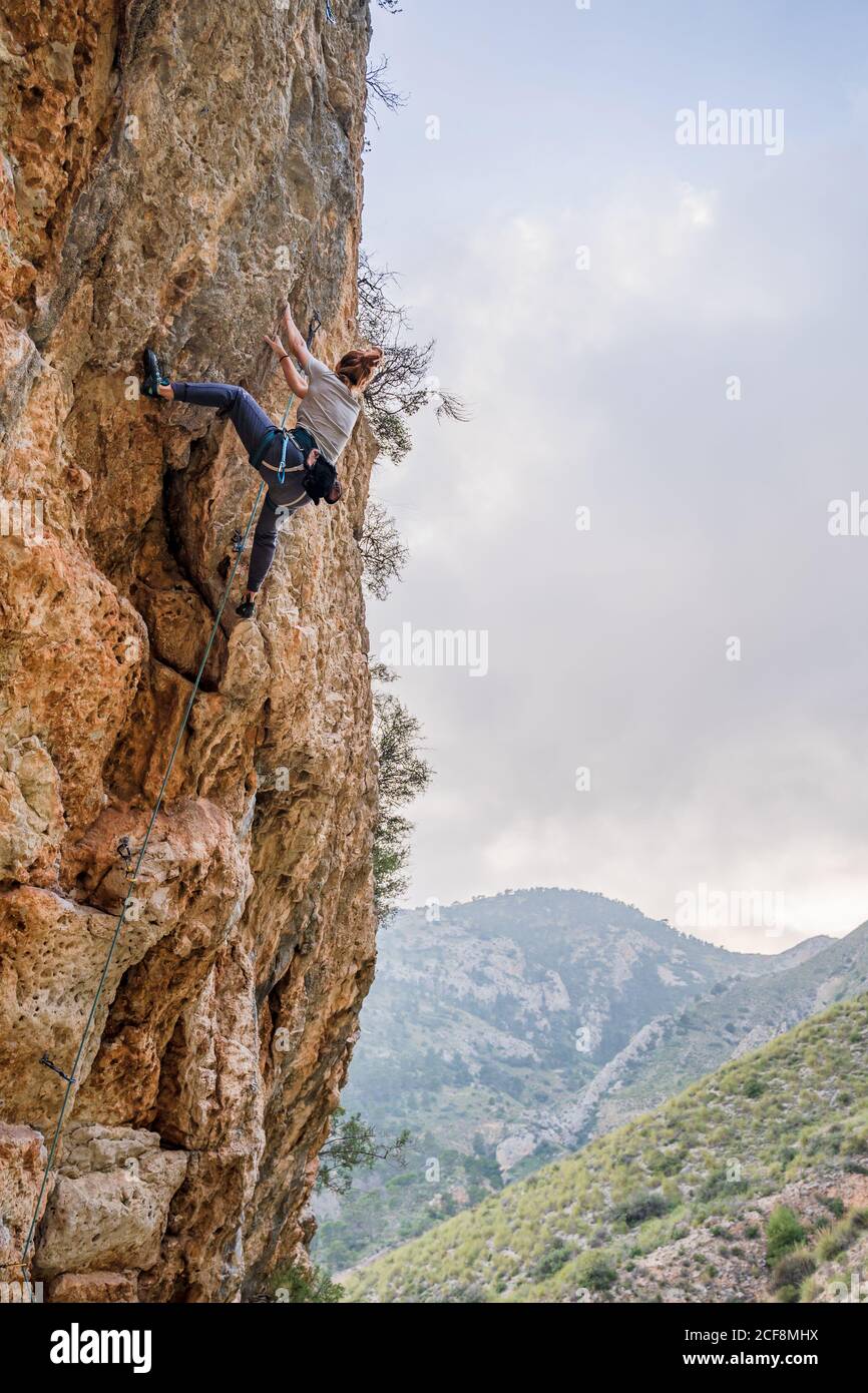 Fearless young female alpinist ascending on vertical cliff in mountain ...