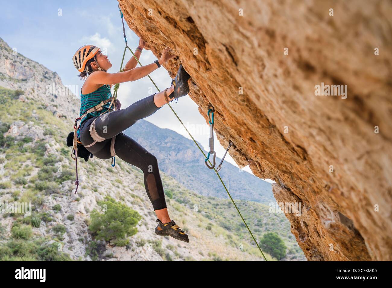 From below of active focused youthful female alpinist climbing on cliff ...
