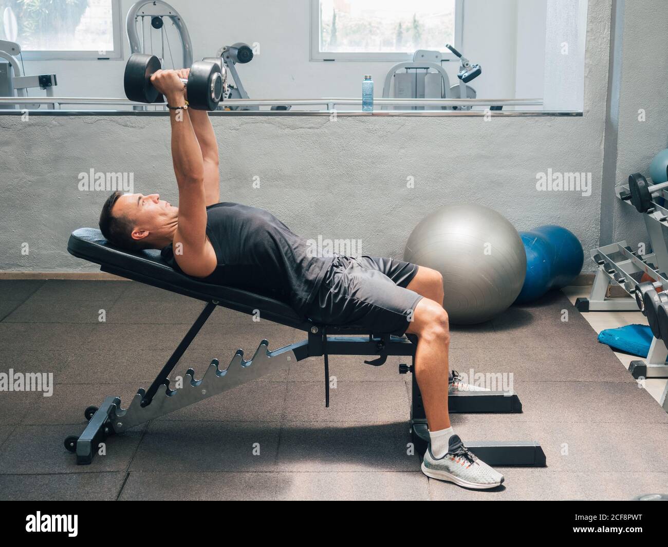 Side view of muscular adult male doing exercise with dumbbells while ...