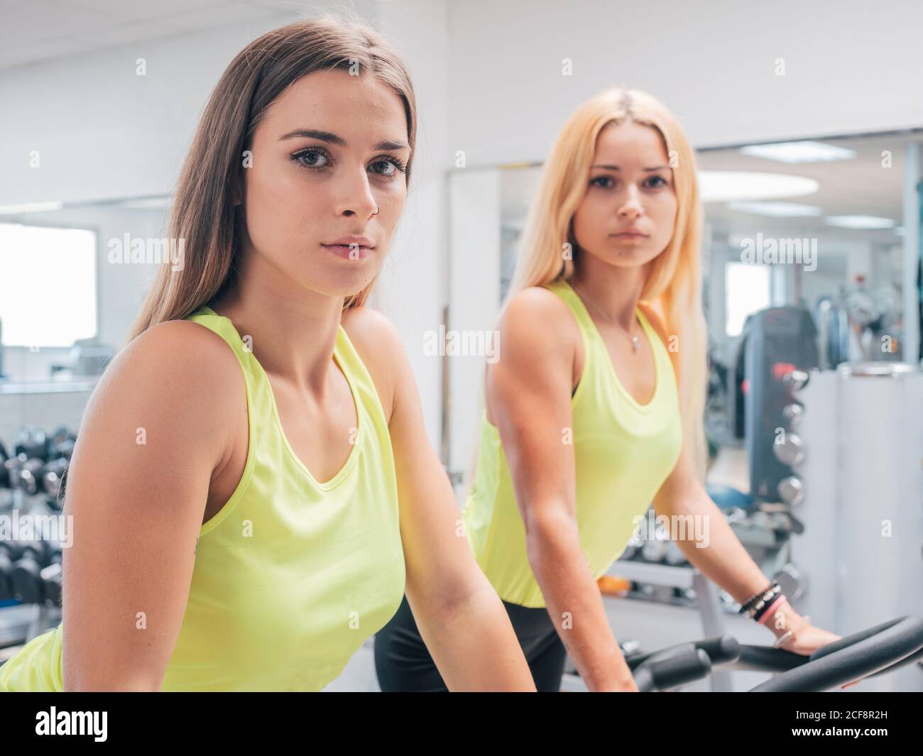 Side view of slim ladies in sportswear training on modern bicycle ...