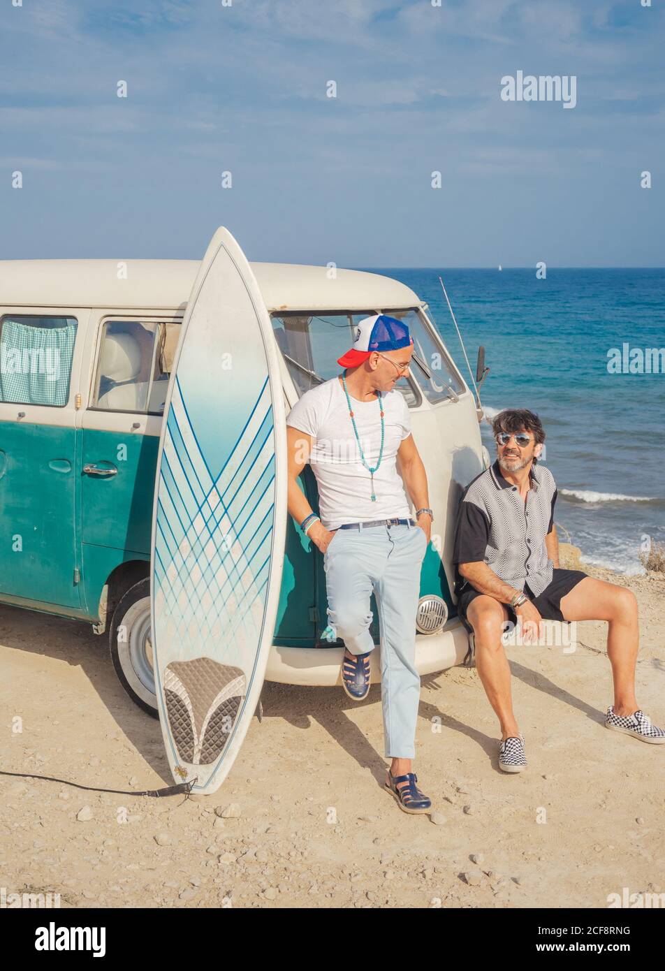 Strong active men with big white surfboard talking near old car on ...