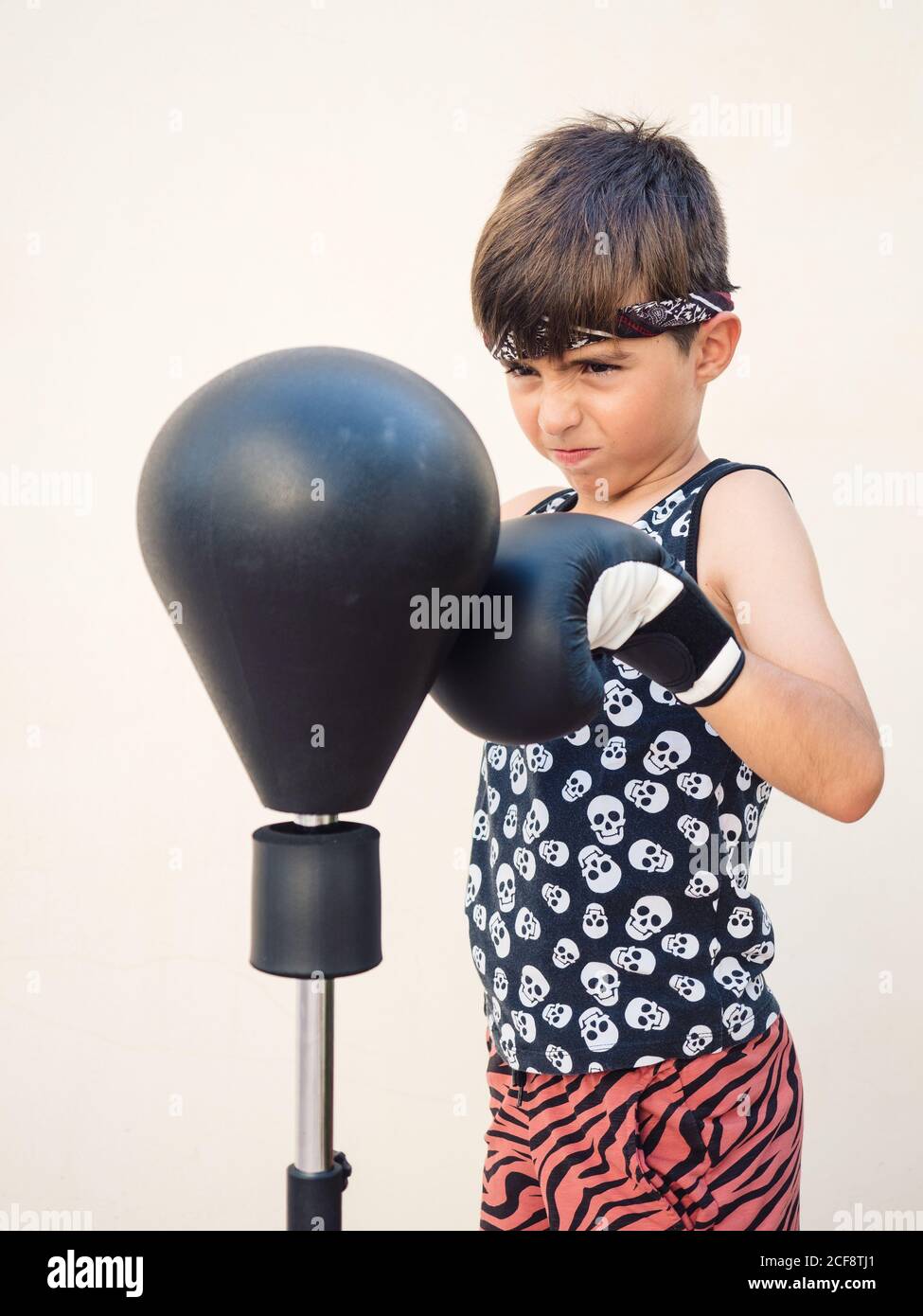 Serious concentrated boy in black boxing gloves beating punch bag with ...
