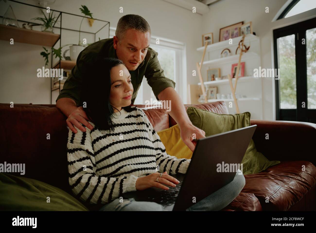 Wife and husband working from home looking at a laptop on the couch ...