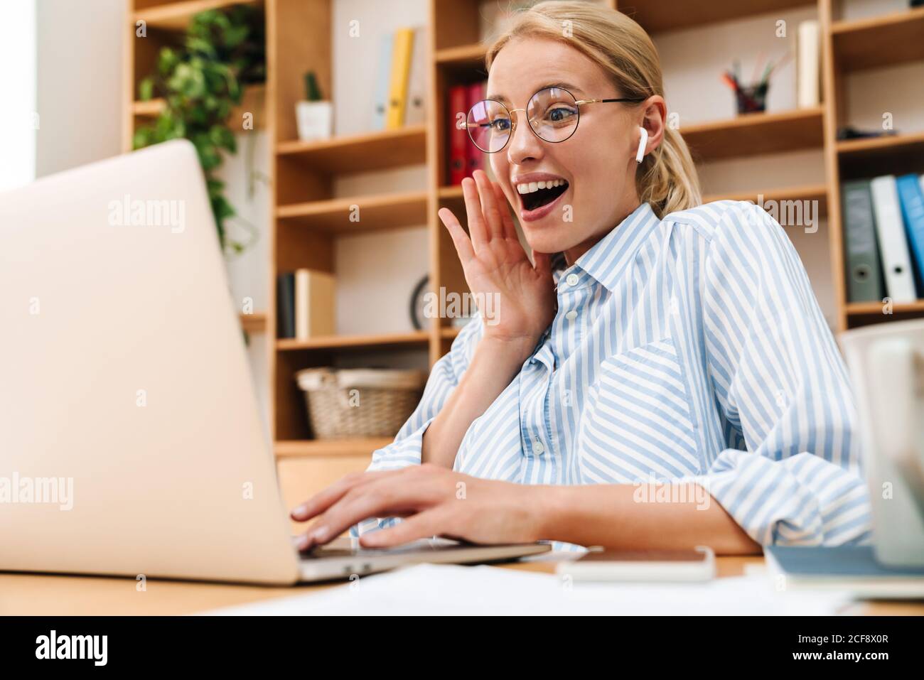 Image of delighted woman using earphones and expressing surprise while ...