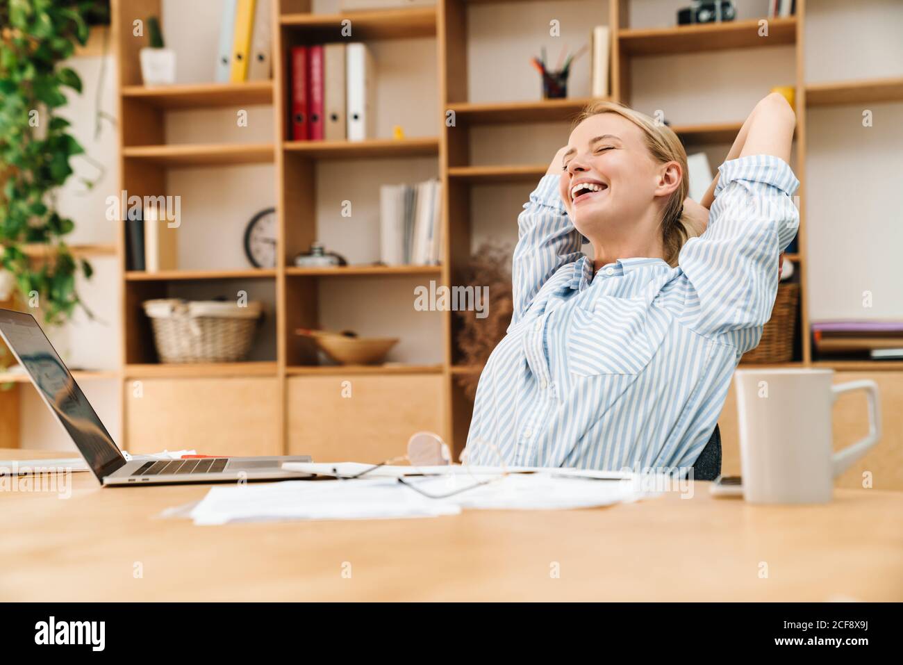 Image of laughing blonde woman stretching her body while working with ...