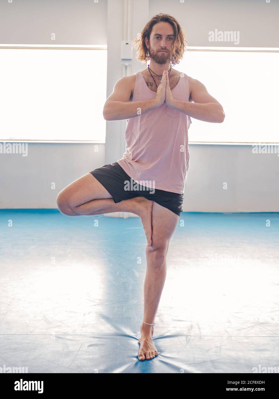 Bearded man in sportswear standing in one leg with prayer hands looking ...