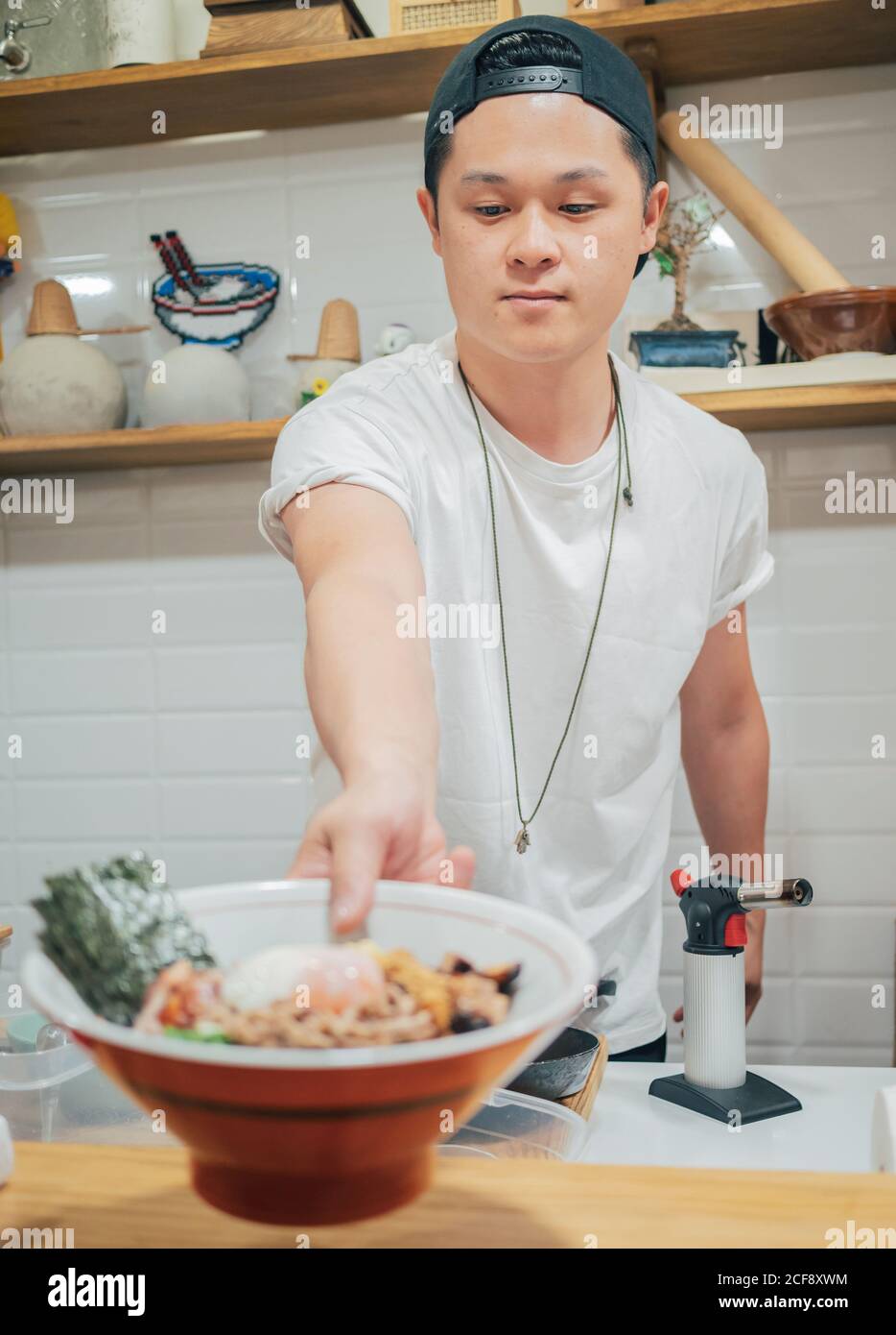 Young male cook putting on counter big bowl with delicious Japanese ...