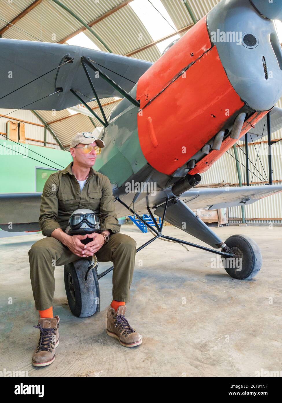 Serious male pilot in uniform sitting beside vintage colorful biplane ...