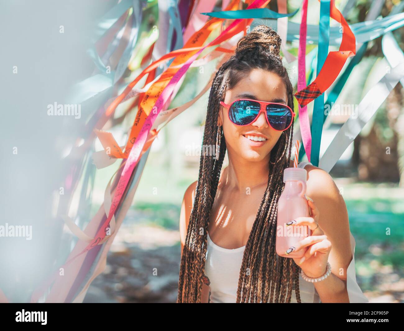 Stylish young female wearing sunglasses dreads drinking cocktail during ...