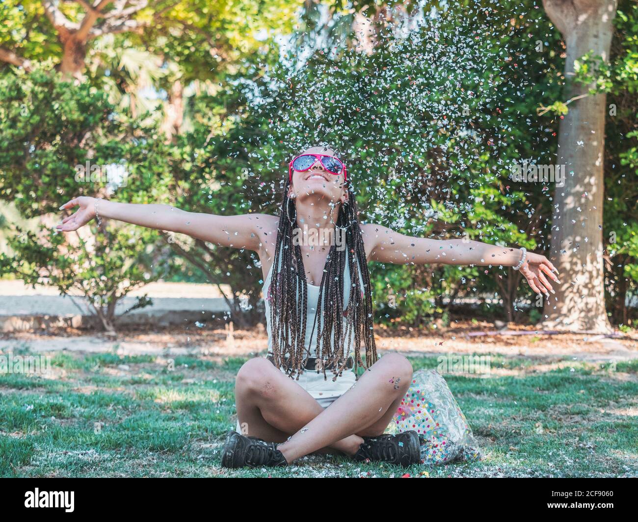 Joyful young female with dreadlocks sitting on ground legs crossed ...