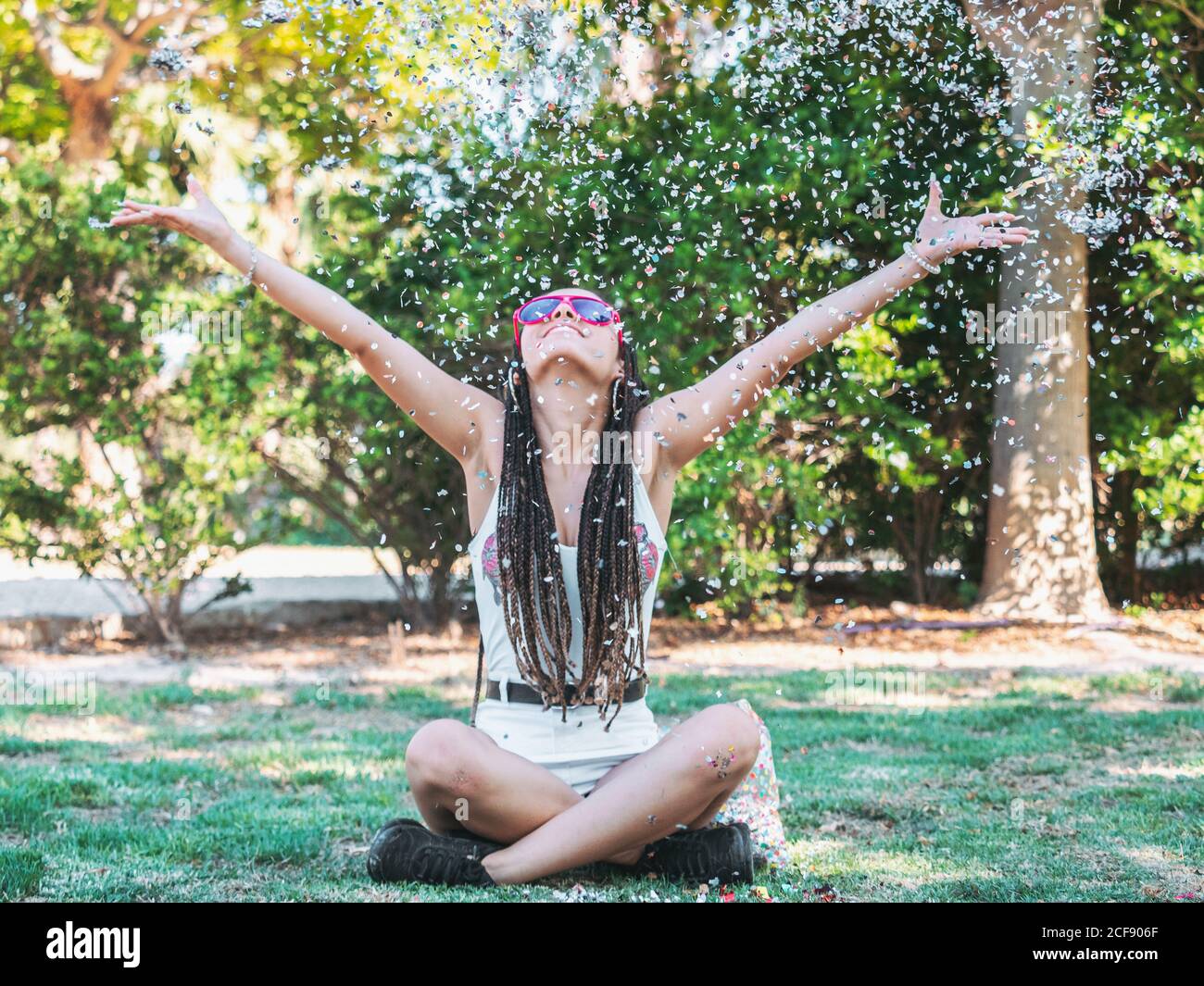 Joyful young female with dreadlocks sitting on ground legs crossed ...