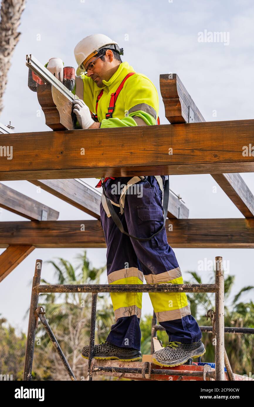 From below of male technician in work wear standing on scaffolding and ...