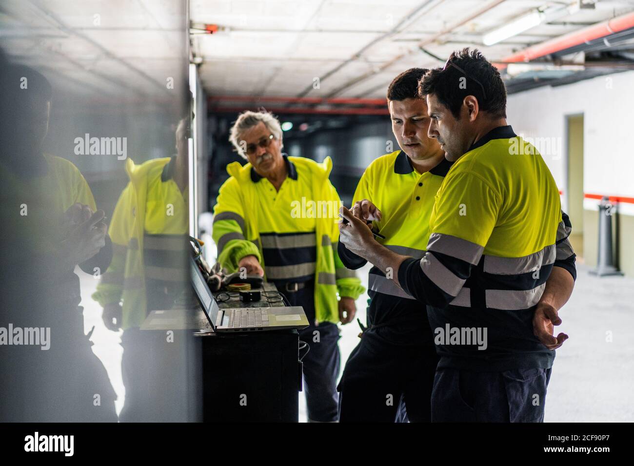 Group of skilled male engineers in uniform using gadgets while ...