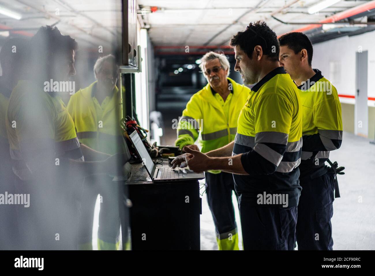 Group of skilled male engineers in uniform using gadgets while ...