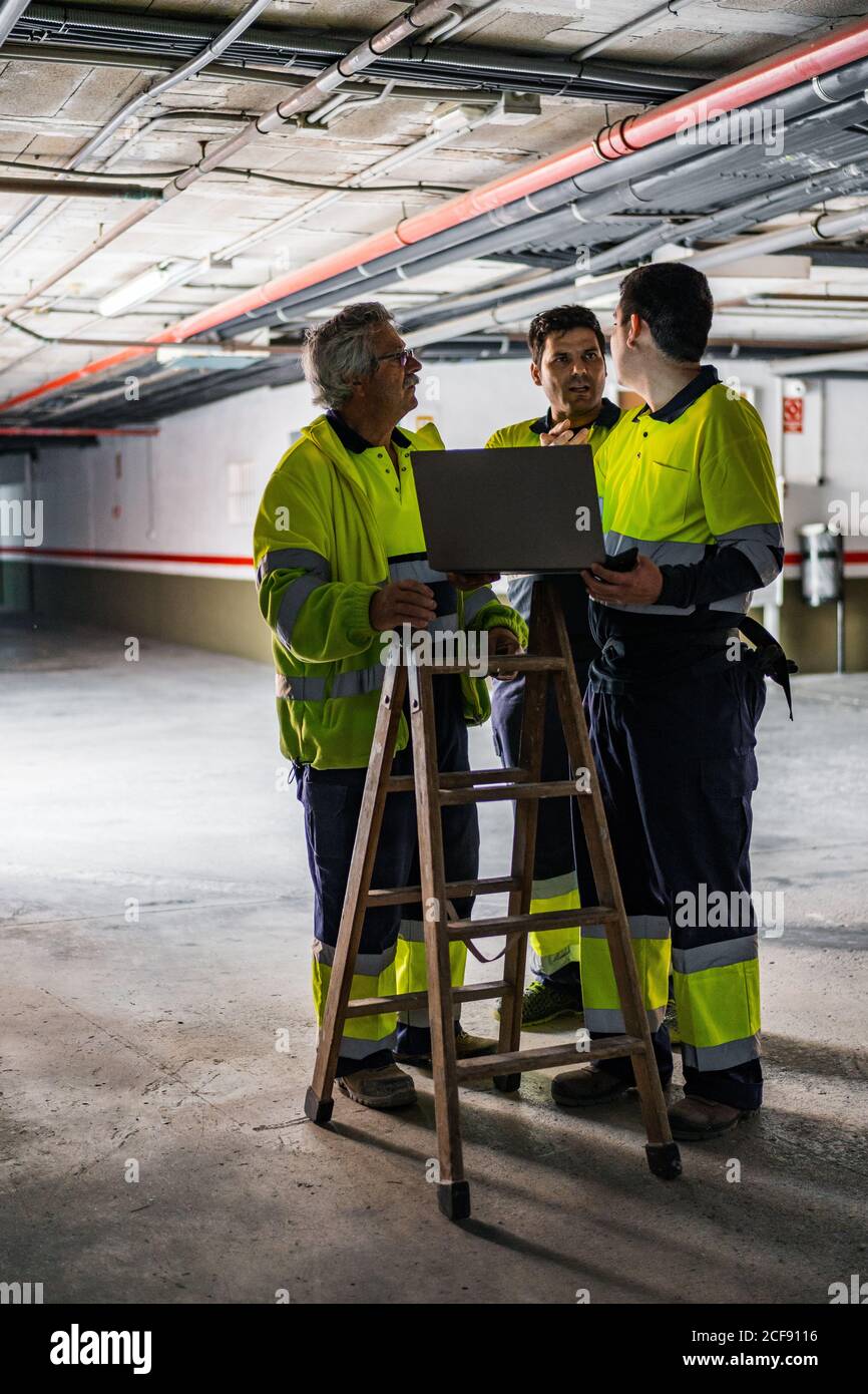 Group of skilled male engineers in uniform using gadgets while ...