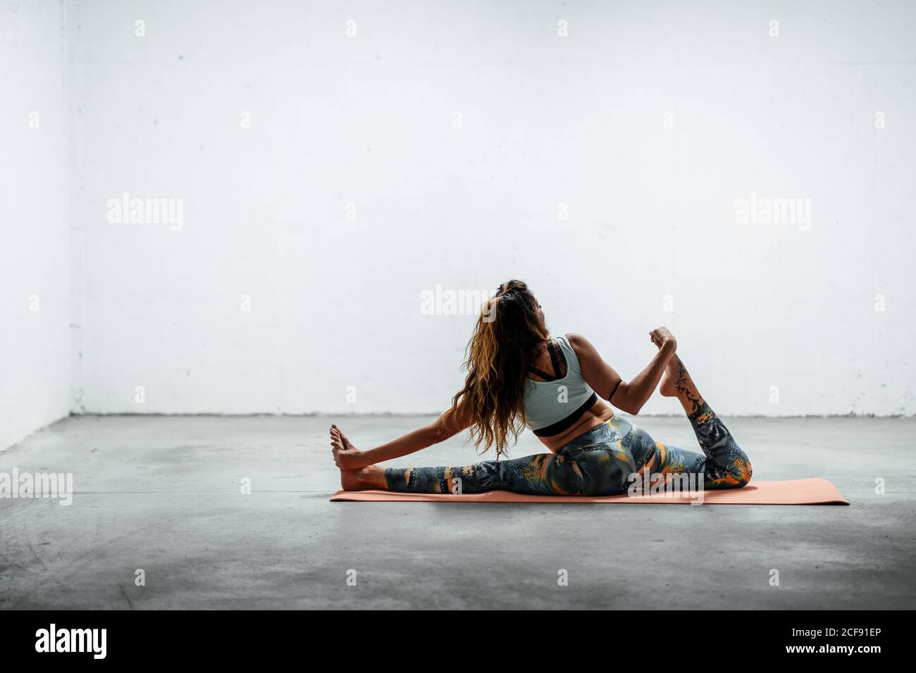 Side view of young flexible female in sportswear doing front split with ...