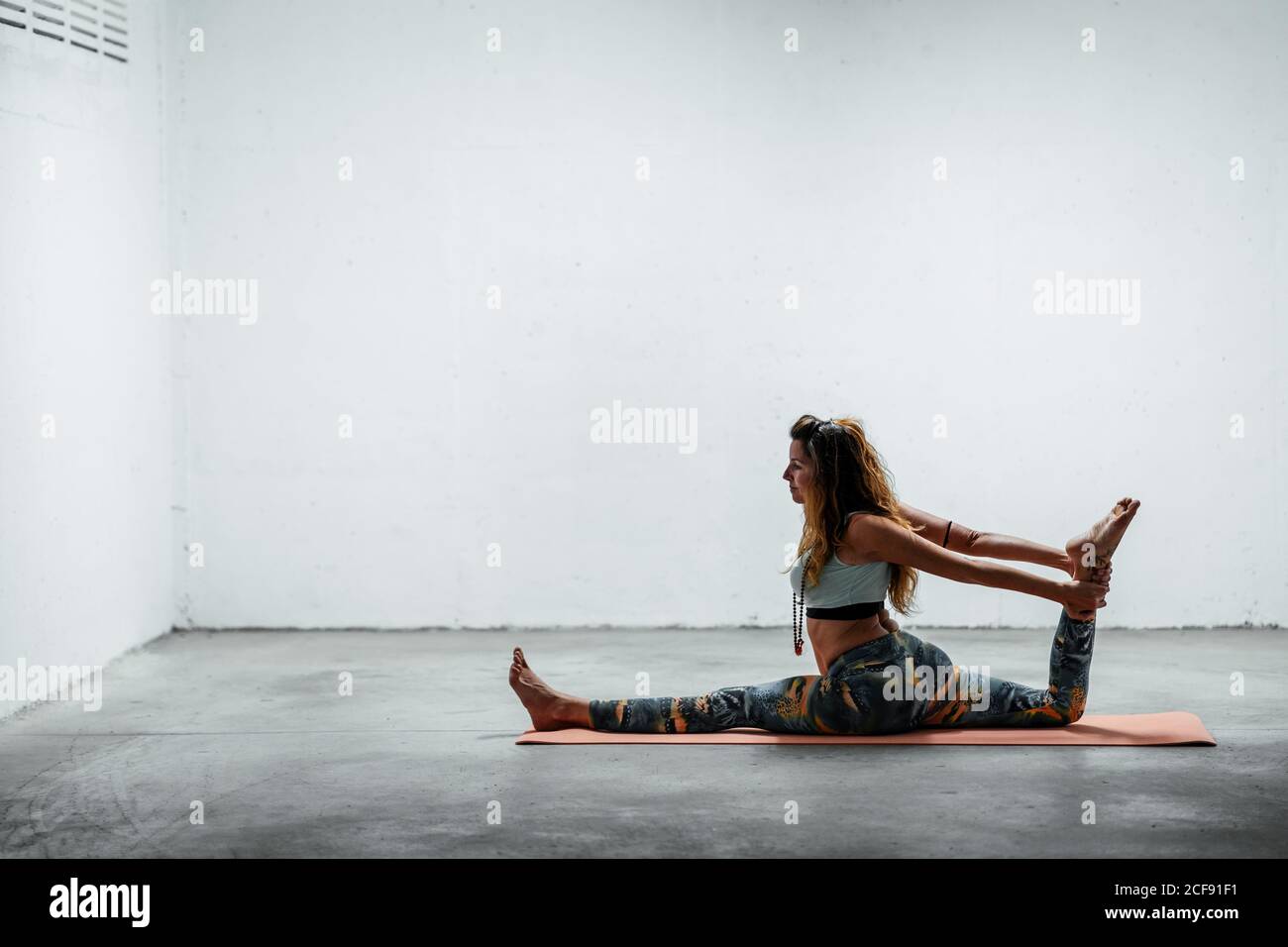 Side view of young flexible female in sportswear doing front split with ...