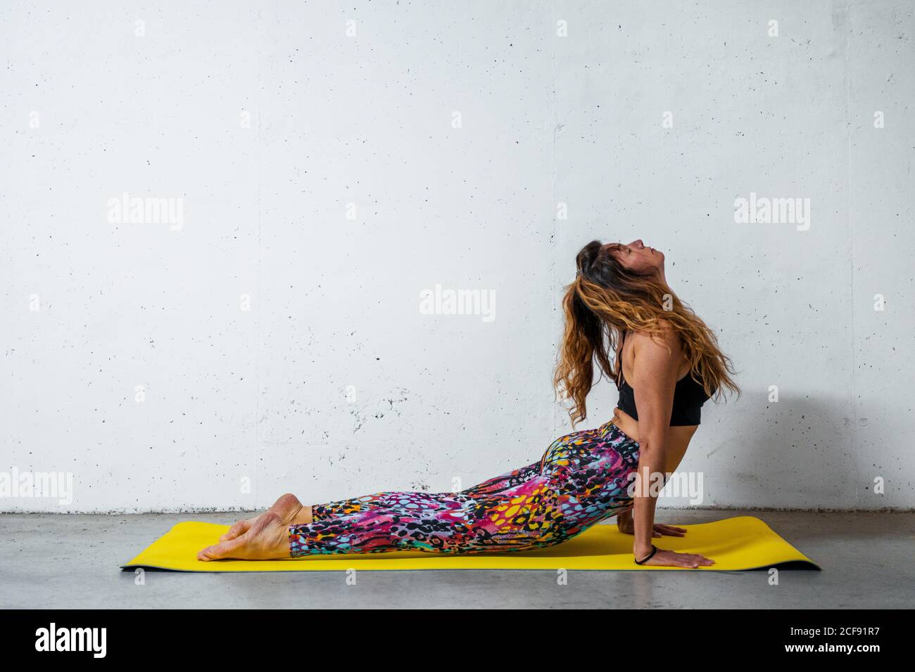Side view of adult Woman in upward facing dog pose against concrete ...