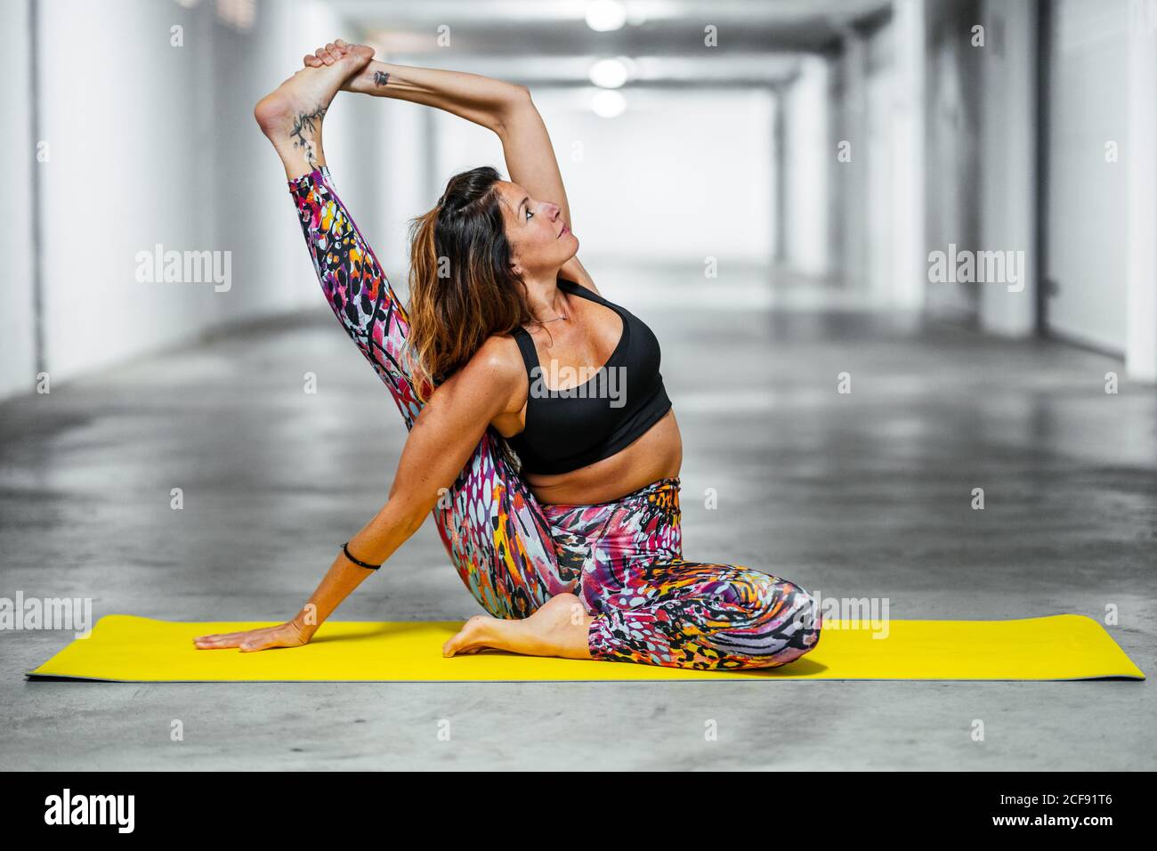 Full body young flexible female in active wear sitting in Compass pose ...