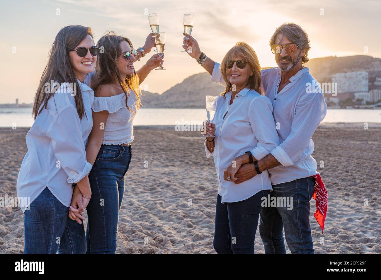 Cheerful mature parents and young daughters clinking glasses of wine ...