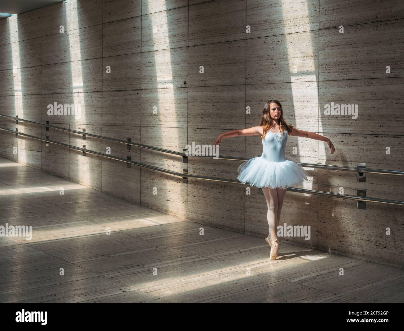 Ballerina in white ballet tutu performing exercises at rail in contrast ...