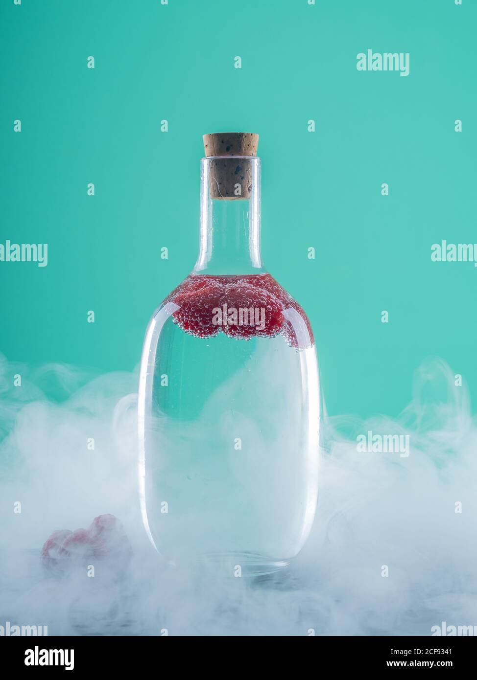 Glass bottle with berries and alcohol on board between mist on azure ...