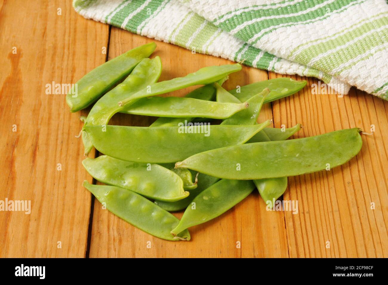 Fresh washed snow peas on a rustic wooden table with a kitchen towel ...