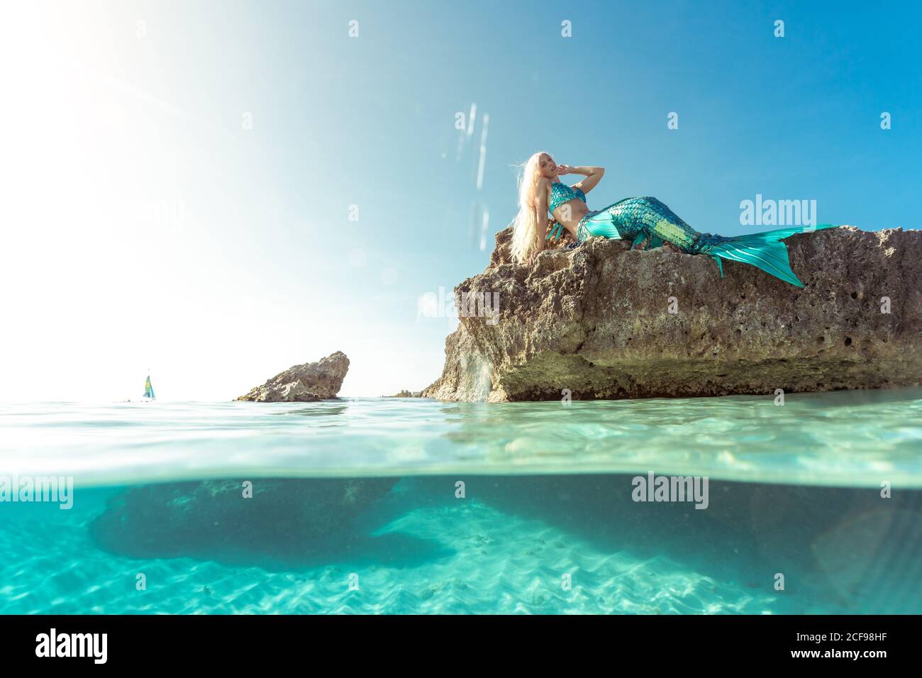 Beautiful young mermaid with blue fishtail relaxing on cliff on sunny ...