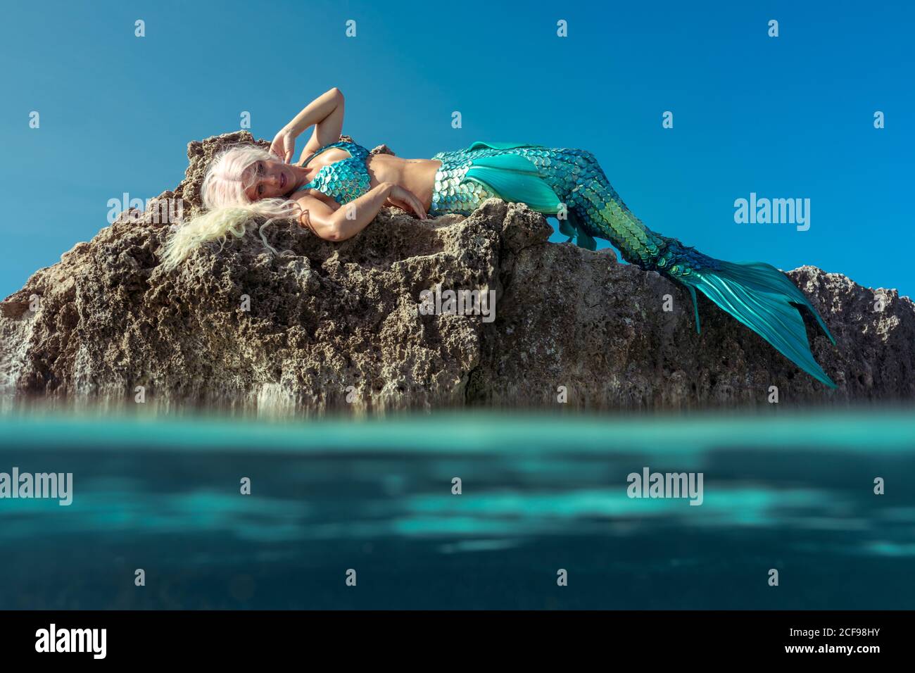 Beautiful young mermaid with blue fishtail relaxing on cliff on sunny ...