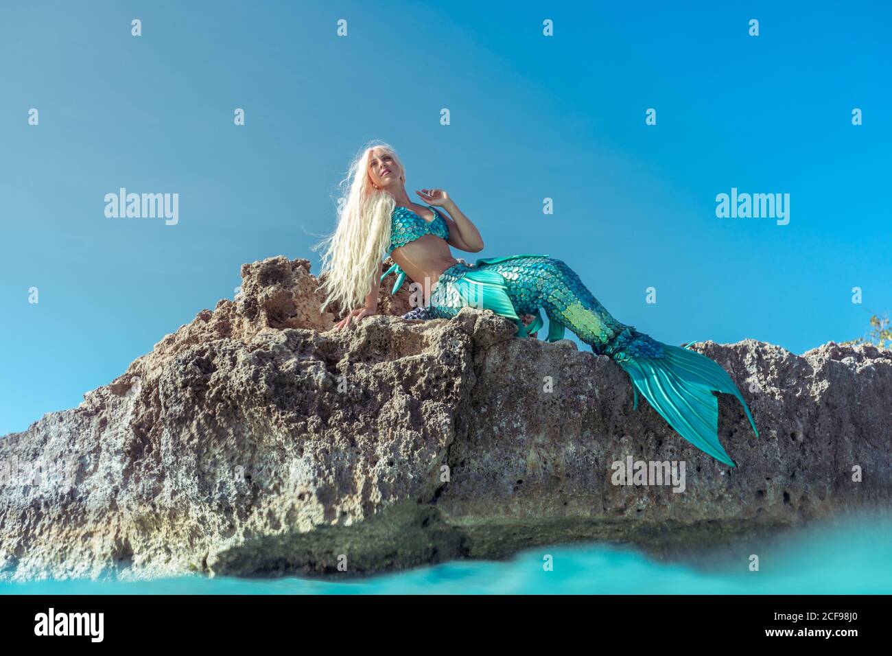 Beautiful young mermaid with blue fishtail relaxing on cliff on sunny ...