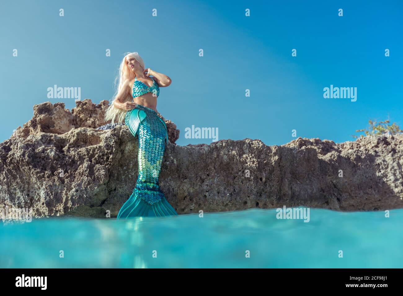 Beautiful young mermaid with blue fishtail relaxing on cliff on sunny ...