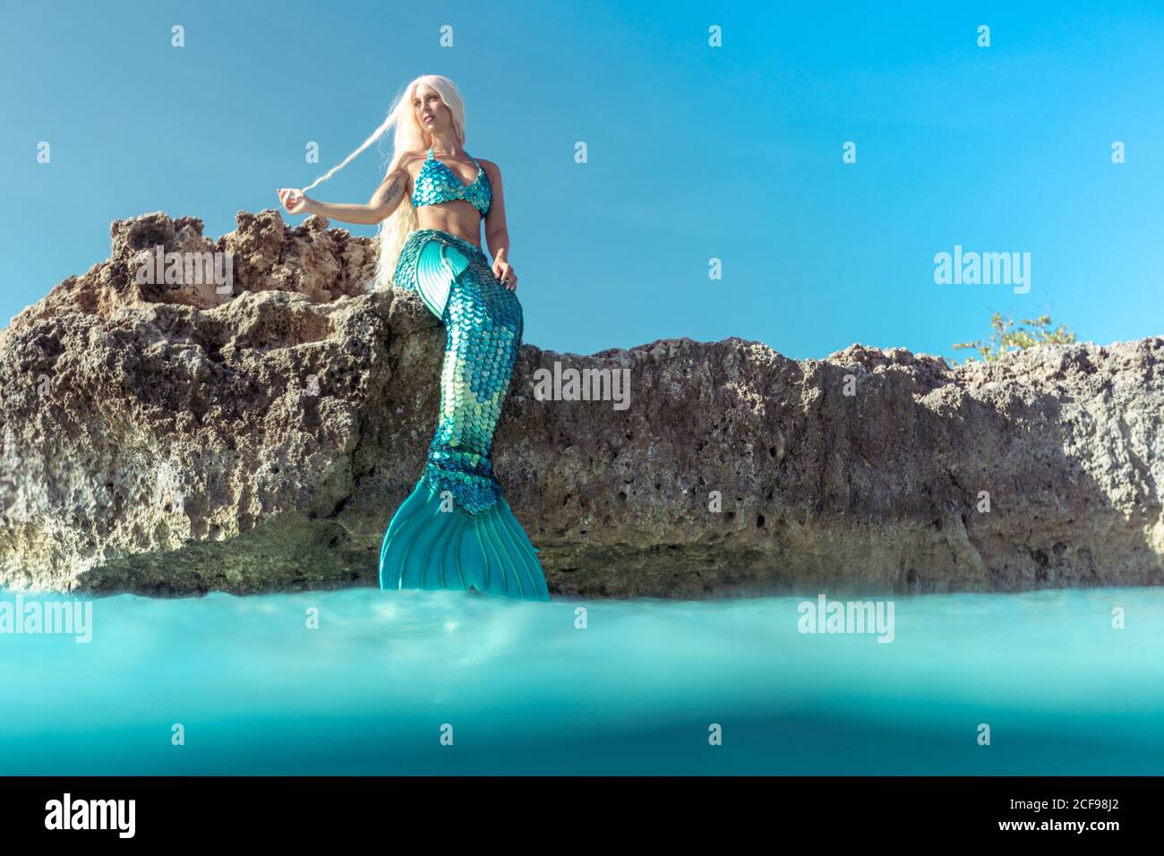 Beautiful young mermaid with blue fishtail relaxing on cliff on sunny ...