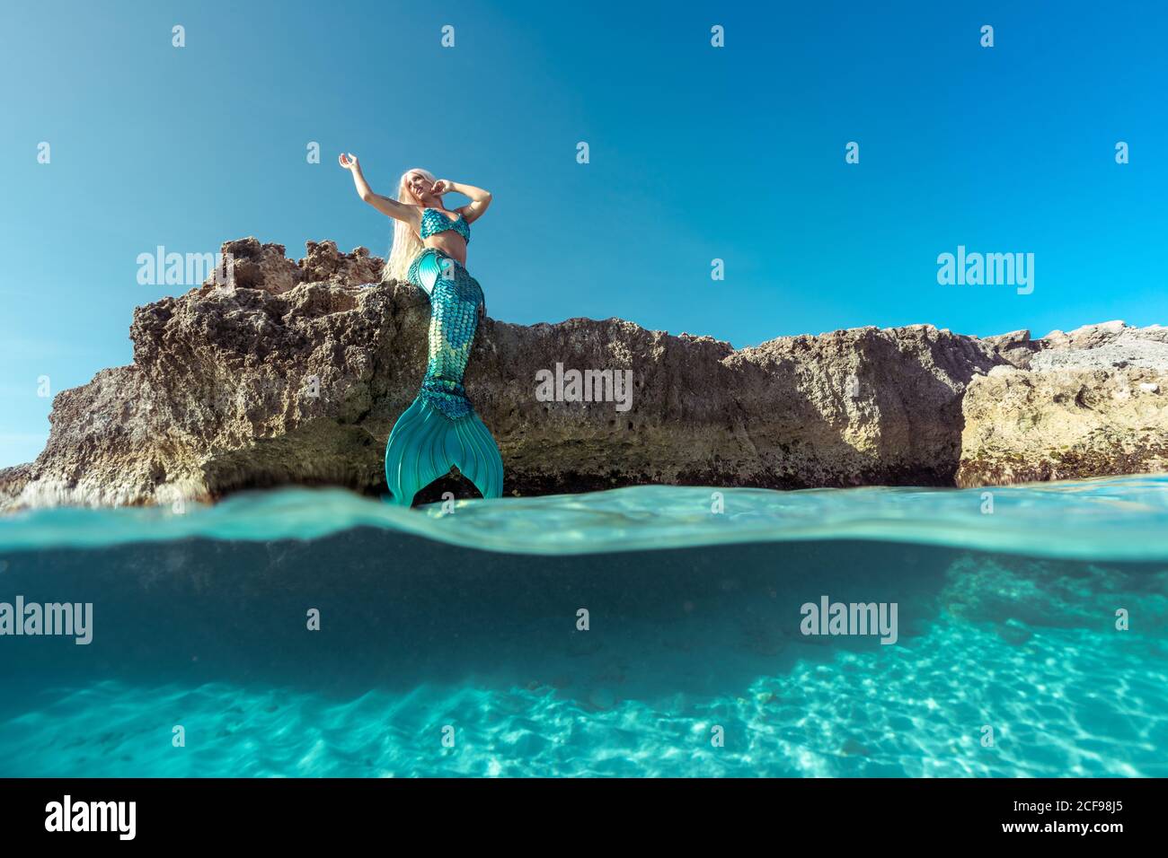 Beautiful young mermaid with blue fishtail relaxing on cliff on sunny ...