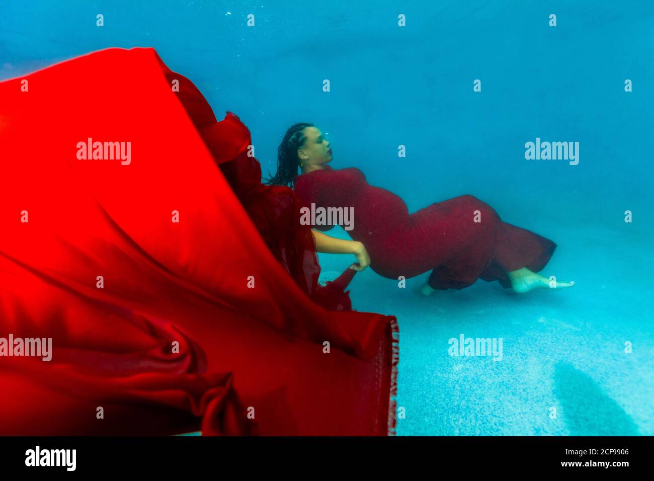 Beautiful pregnant Woman in red dress floating underwater with hands on ...
