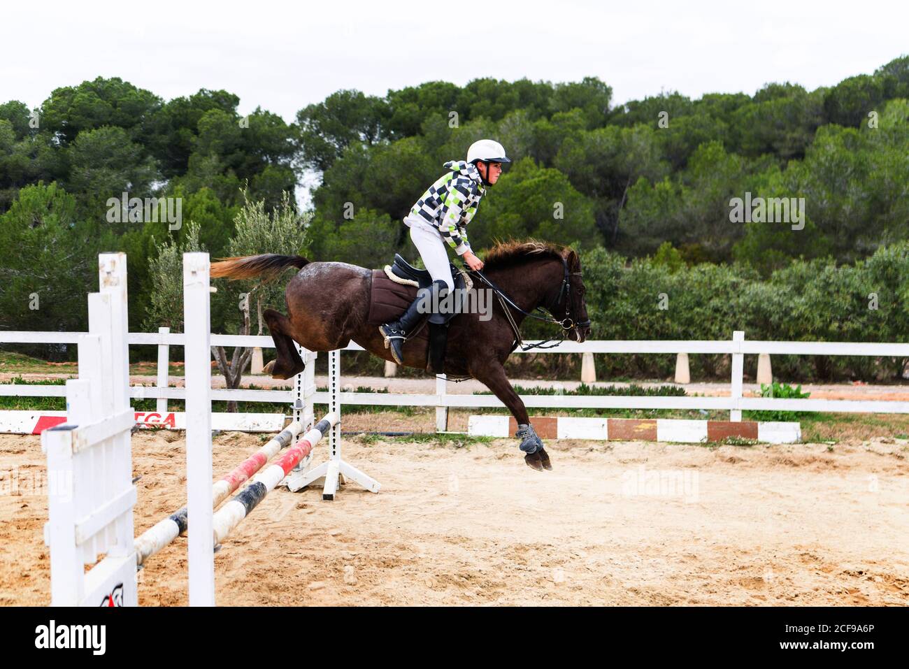 Side view of teen boy in helmet sitting on horse back and jumping over ...