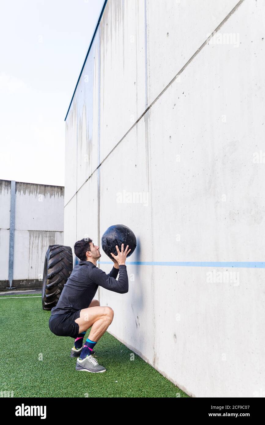 Side view of young athletic male tossing heavy training ball near tire ...