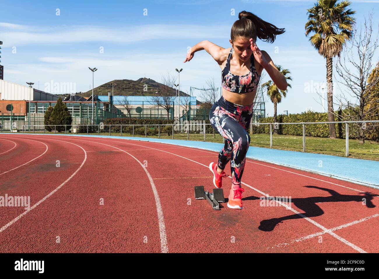 Strong female athlete in sportswear running fast against blue sky on ...