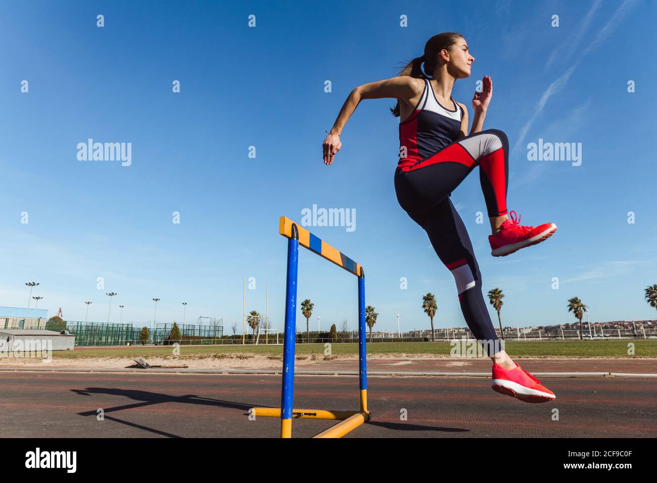 Side view of strong young Woman in sportswear leaping over hurdle ...