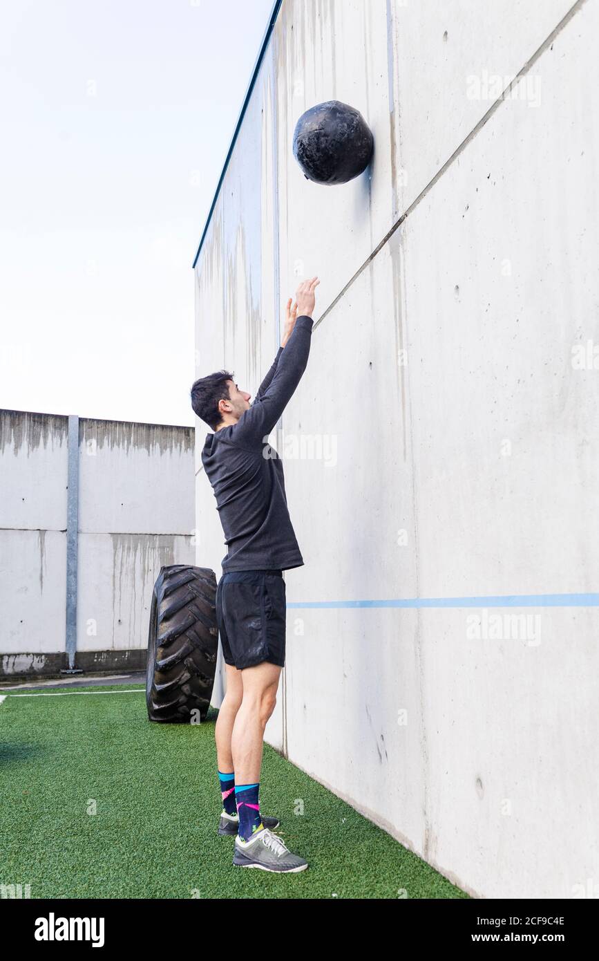 Side view of young athletic male tossing heavy training ball near tire ...