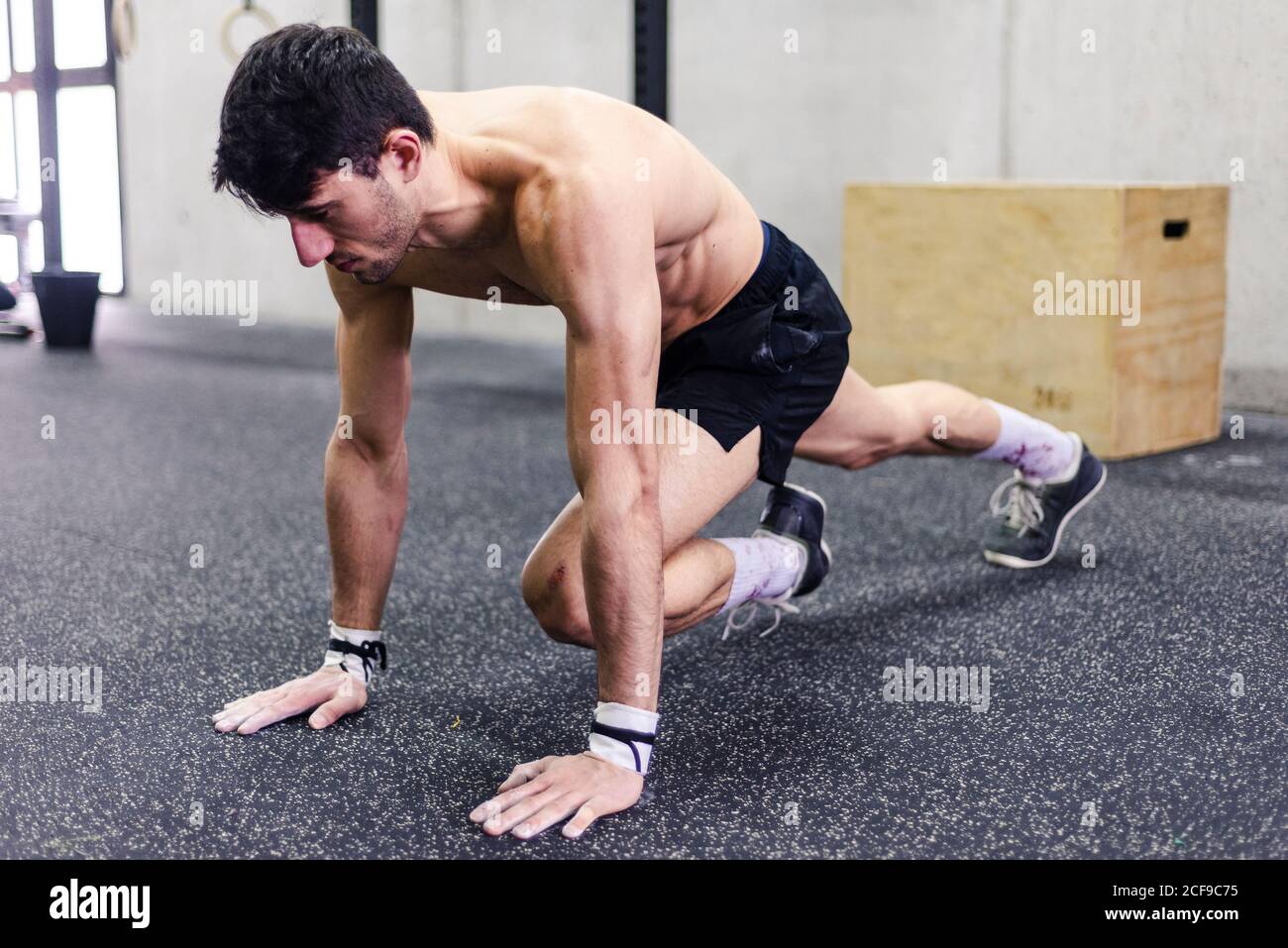 Young shirtless male doing plank and stretching legs near grey wall in ...
